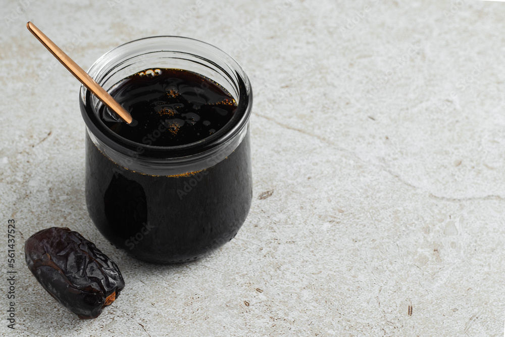Date syrup in a glass jar, spoon, whole date fruit. Close up. Beige ...