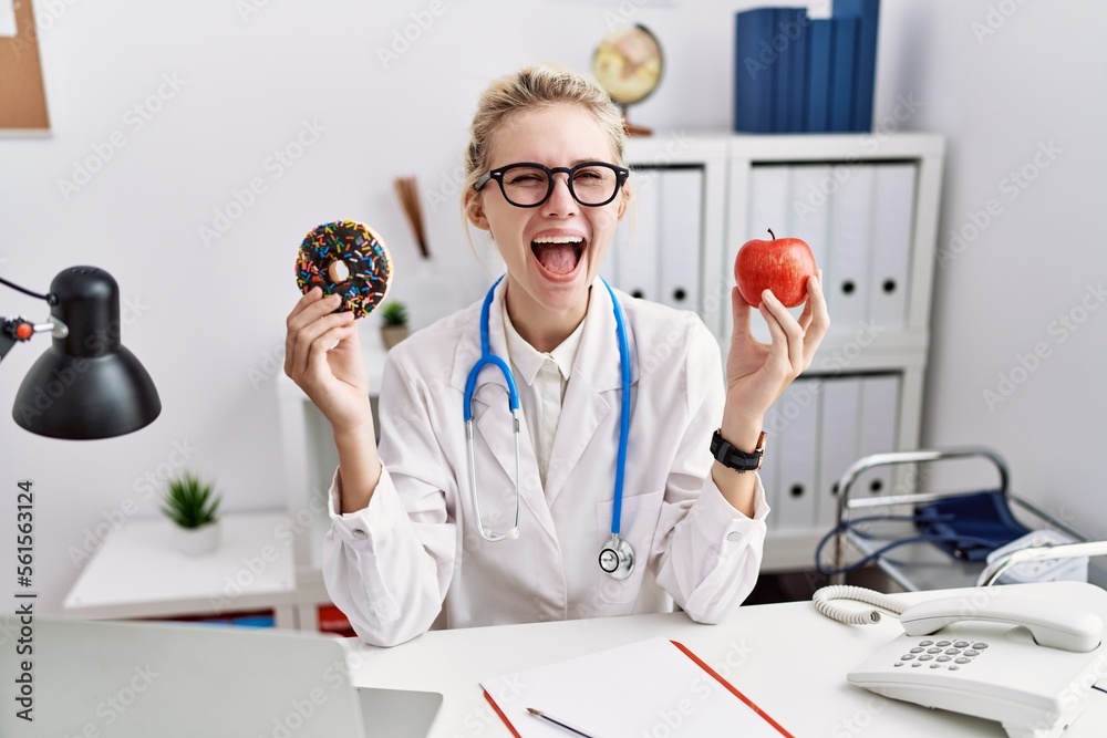 Young doctor woman holding red apple and donut at the clinic ...