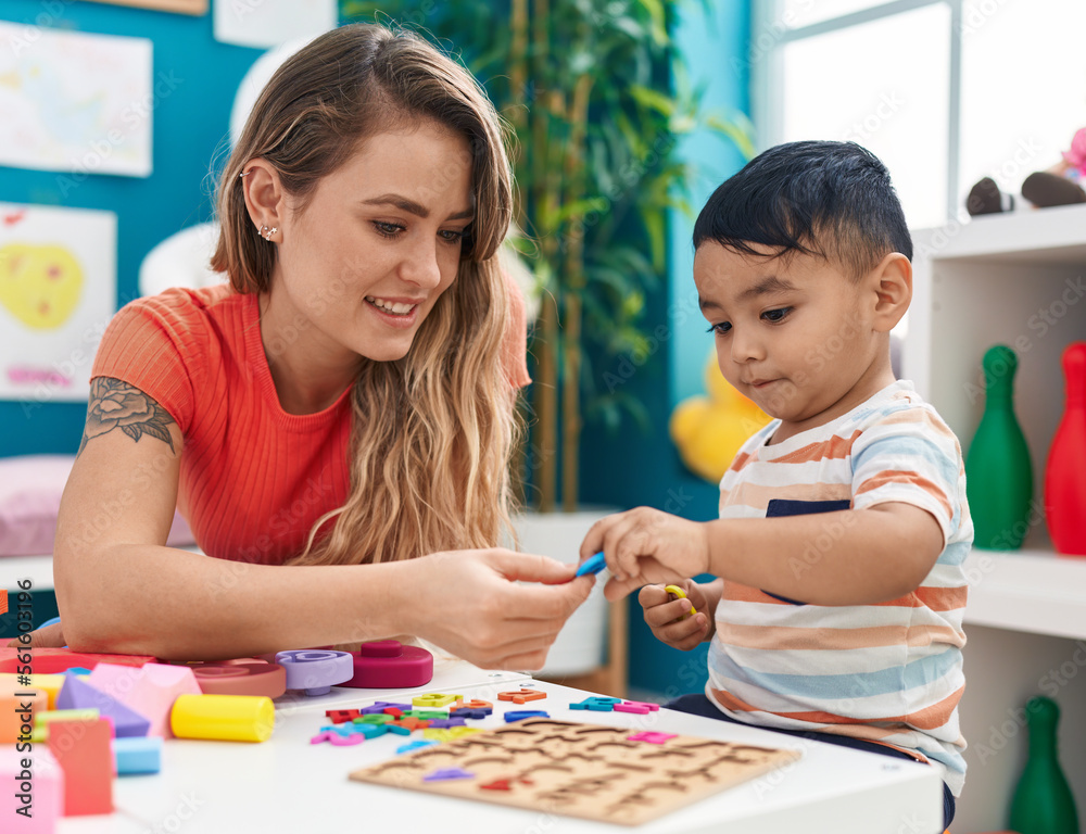 Teacher and toddler playing with maths puzzle game sitting on table at ...