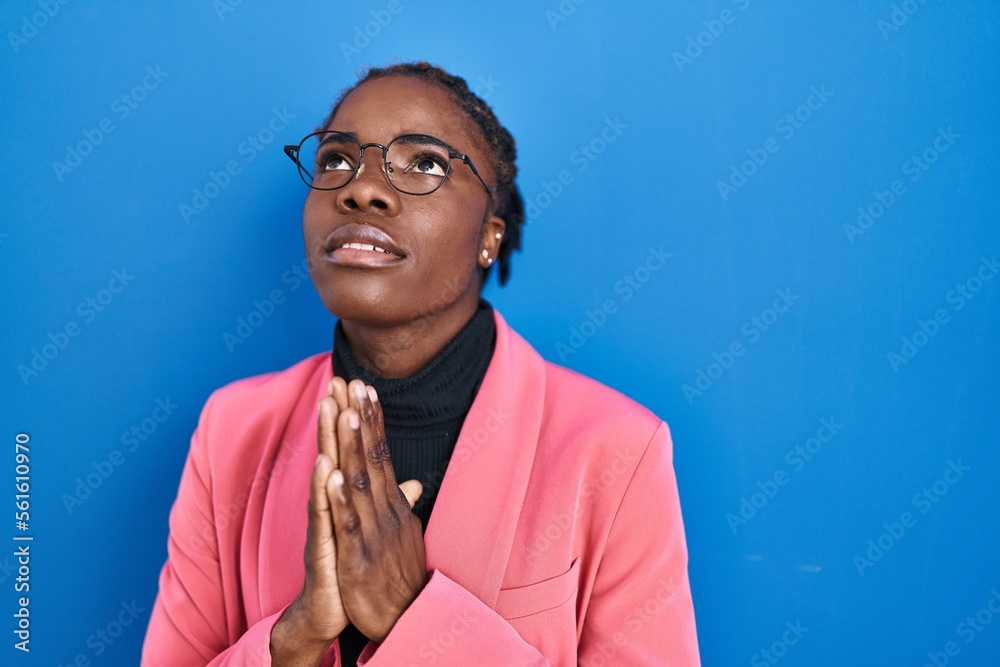 Beautiful black woman standing over blue background begging and praying ...