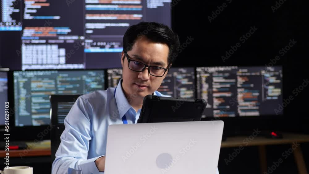 Asian Male Programmer Using Tablet While Writing Code By A Laptop Using ... Asian Male Programmer Using Tablet While Writing Code By A Laptop Using ...
