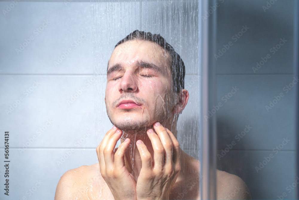 Portrait of young man bare shoulders standing under shower eyes closed ...