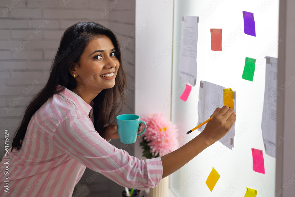 Portrait of a young woman writing on sticky note over a glass wall in ...