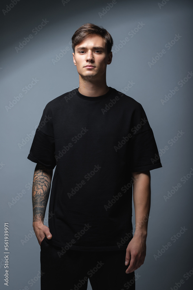 A guy of model appearance in black clothes poses on a gray studio ...