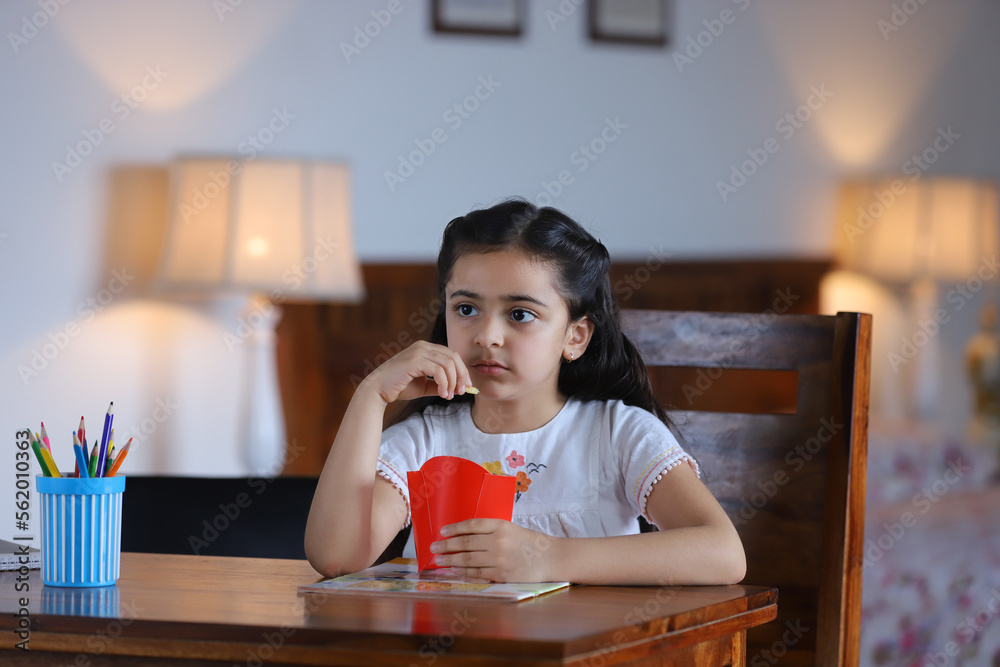 Thoughtful little Indian girl thinking while eating french fries ...
