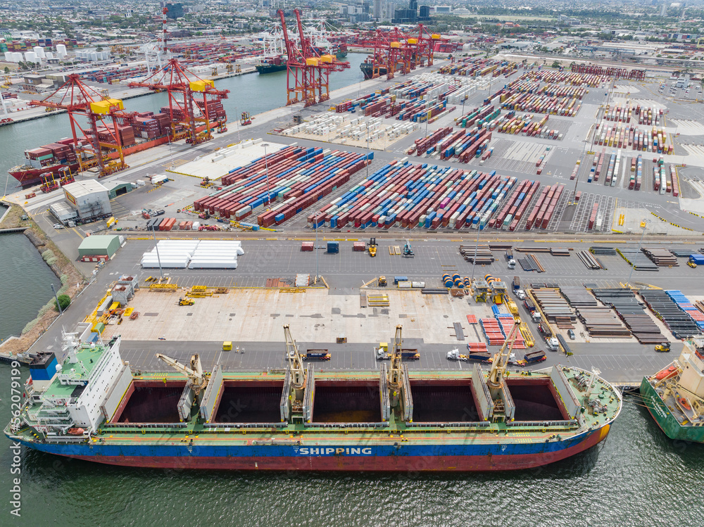 Aerial view of a cargo ship with its holds open at wharf lined with ...