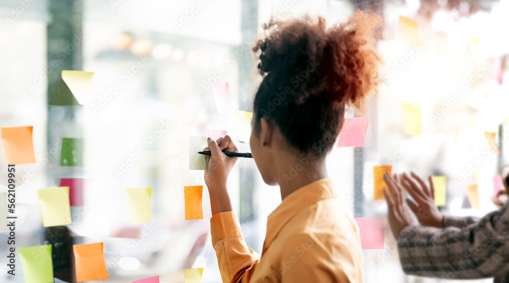Young businesswoman creative team using post it notes in glass wall to ...