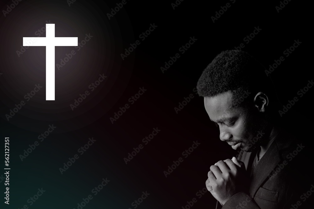 African man in suit is praying and giving thanks to god in dark room ...