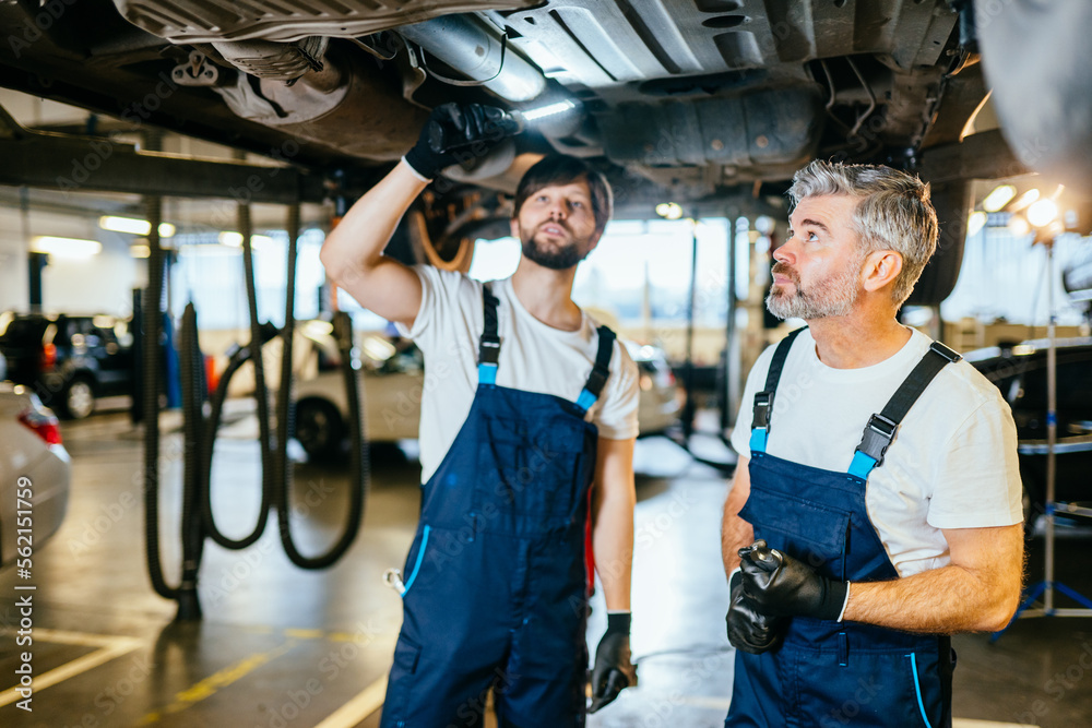 Two auto mechanics men in uniform at car suspension repair work ...