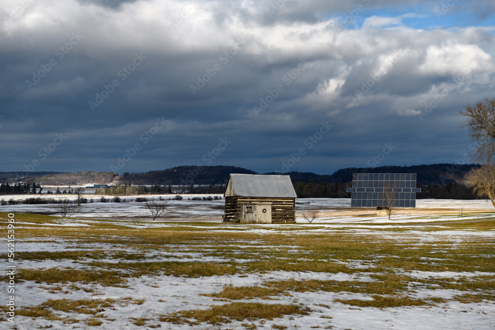 Log cabin shotgun shack with solar panel in farmers field with snow and ...