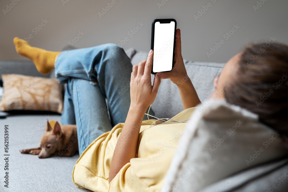 Female person holding smart phone in hands while lying down on sofa at ...