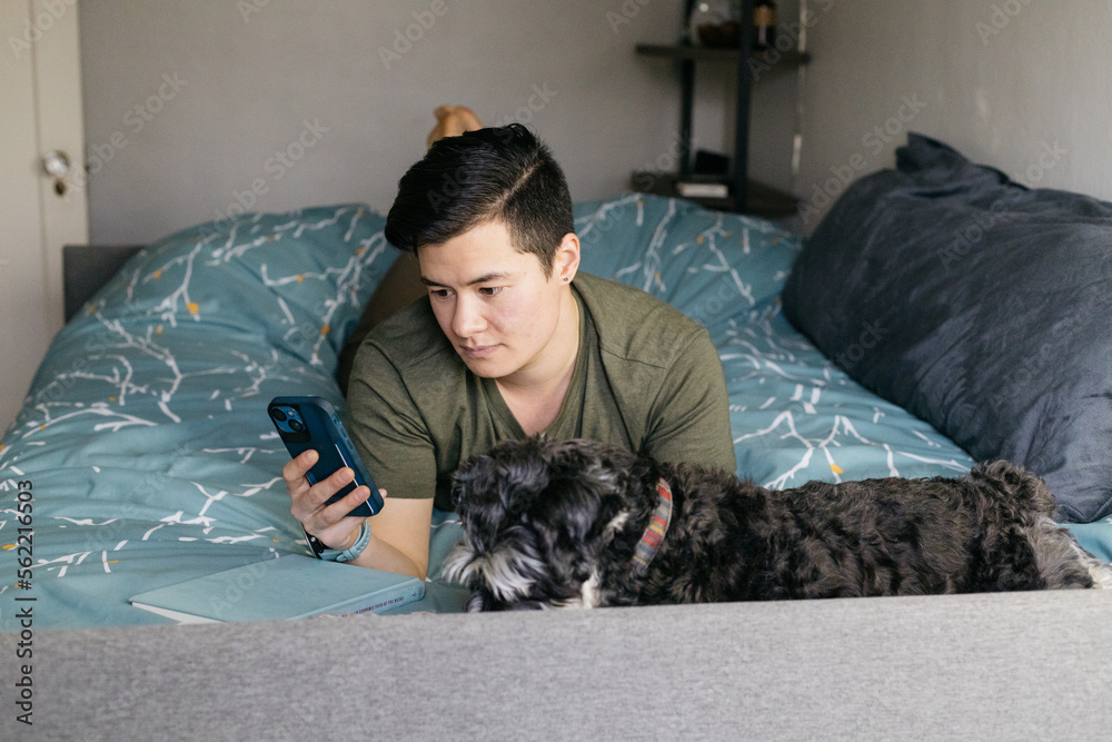 a transgender man at home with his dog on phone. Stock Photo | Adobe Stock