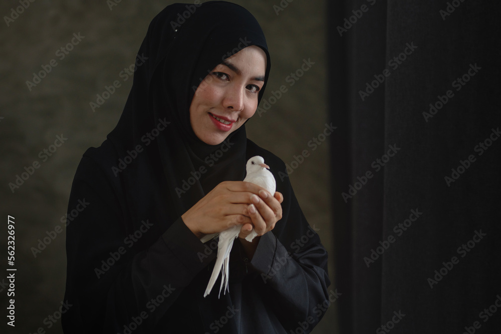 Muslim woman in black hijab tenderly holds a white bird in her hands ...