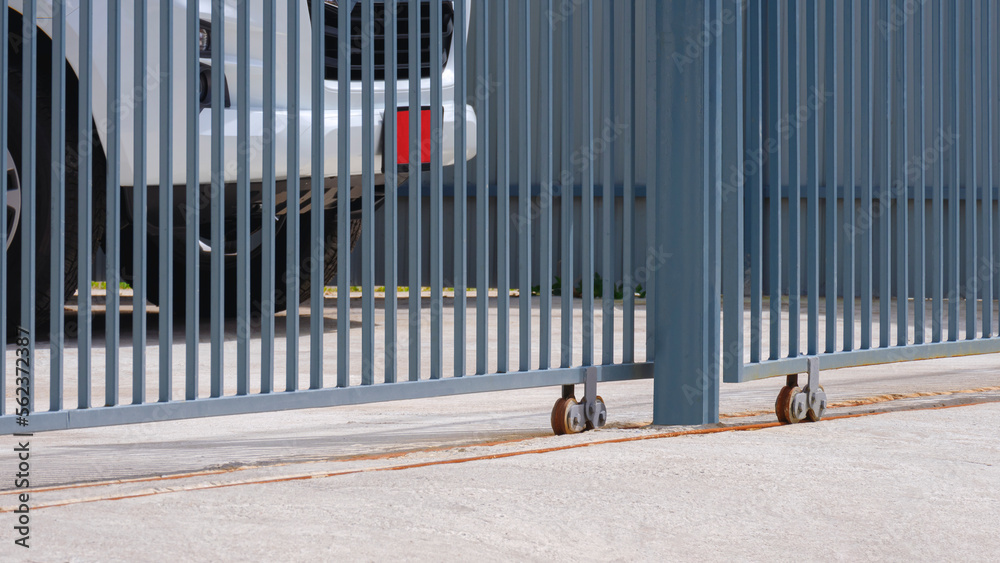 Perspective side view of sliding steel fence gate with white car parked ...