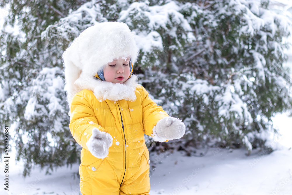 child playing with snow. portrait of little girl in yellow jumpsuit and ...