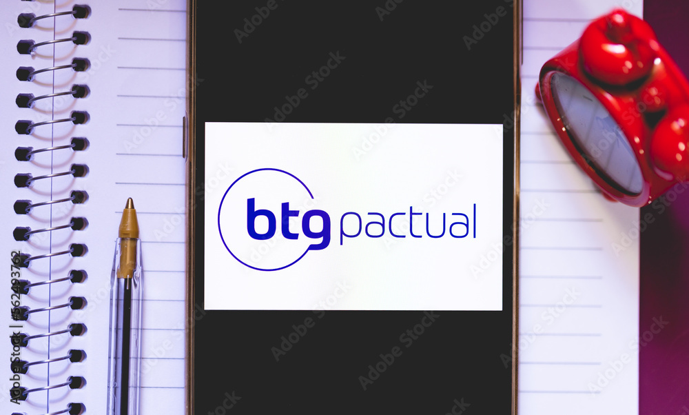 A logo do banco BTG Pactual na tela de um telefone celular. Um caderno ...