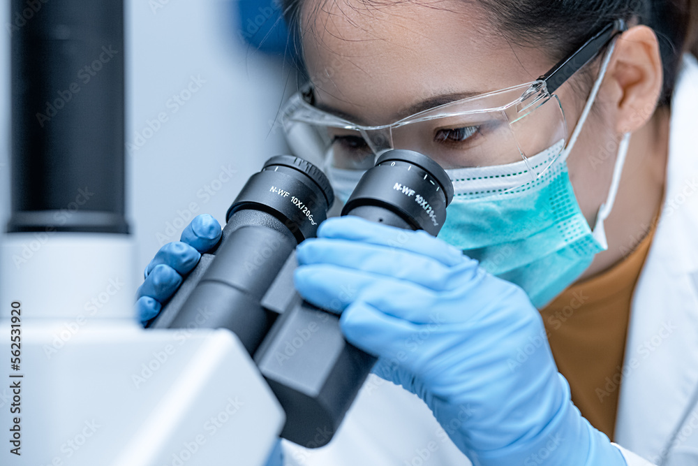 Closeup shot of a female researcher wearing safety goggles looking with ...