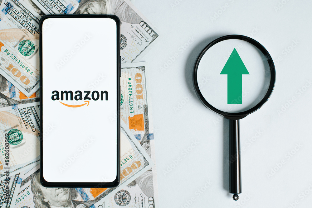 Amazon logo on screen of mobile phone, pile of dollars money ...