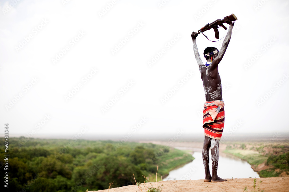 A young man holds his kalashnikov rifle over his head while overlooking ...