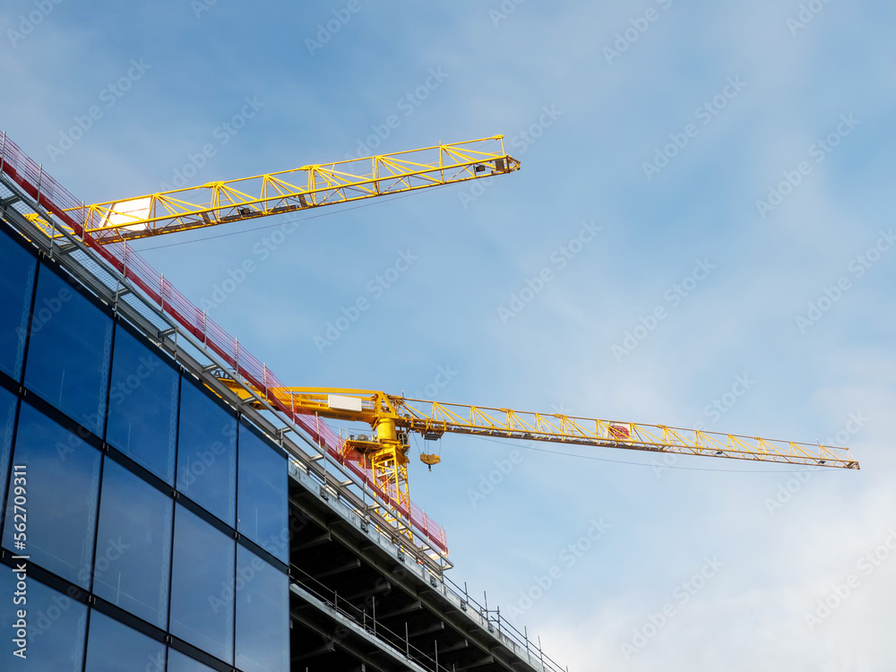 Two cranes against blue cloudy sky and part of a modern building at ...