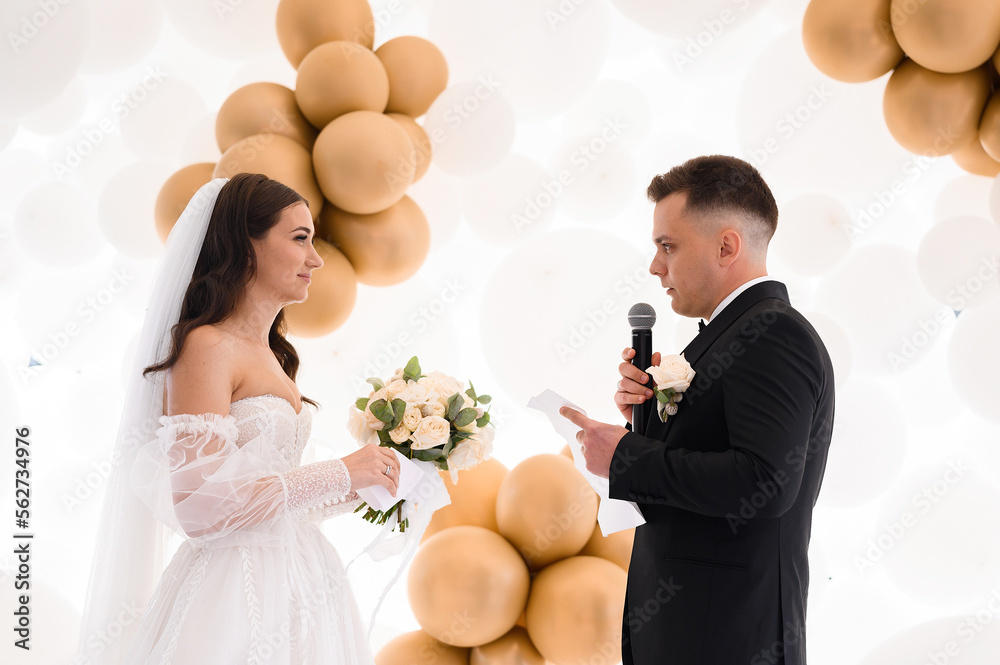 Side view of serious groom in suit, which picking up microphone and ...