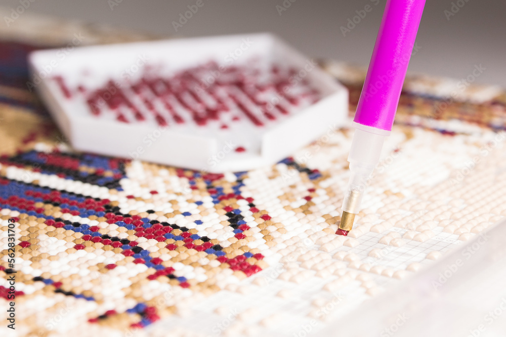 The moment of gluing a red rhinestone with a stylus onto a diamond ...
