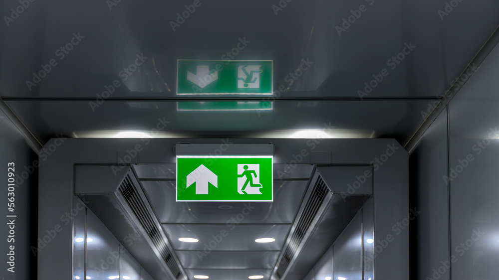 Green emergency exit sign showing the way to escape. Fire exit in the ...