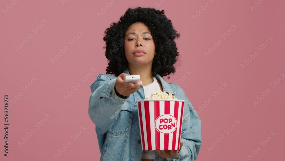 Serious woman of color watching TV for entertainment using remote ...