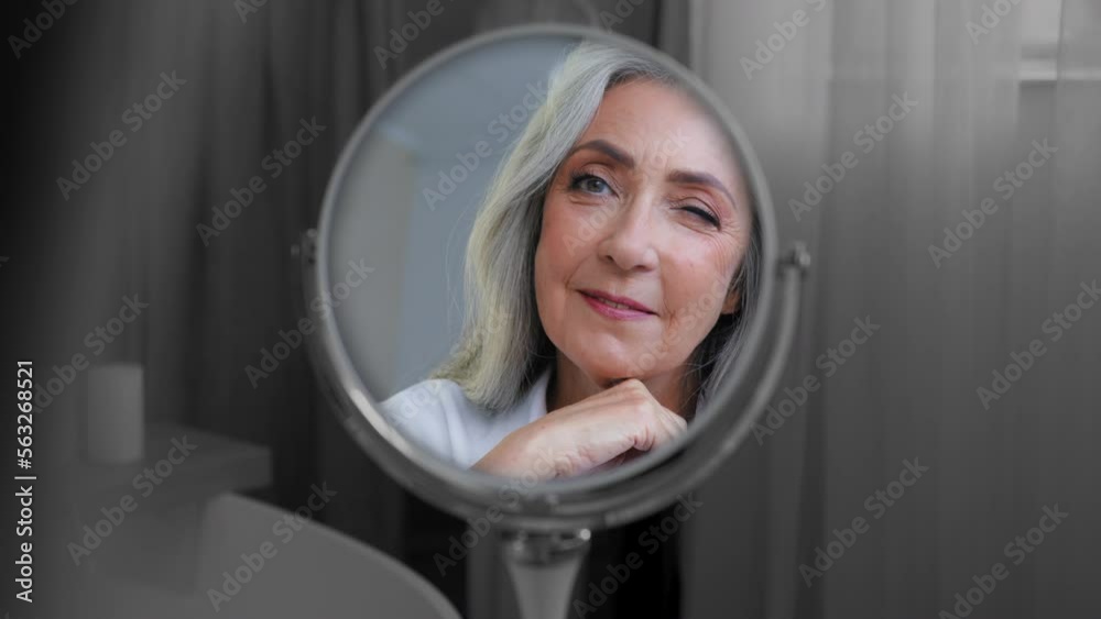 Mirror reflection female wrinkled smiling face of old Caucasian woman ...