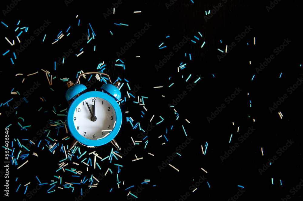 Classic arrow blue alarm clock on black background and blue sprinkles ...