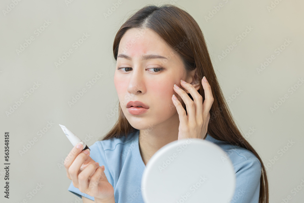 Dermatology, asian young woman looking at mirror, holding cream tube in ...