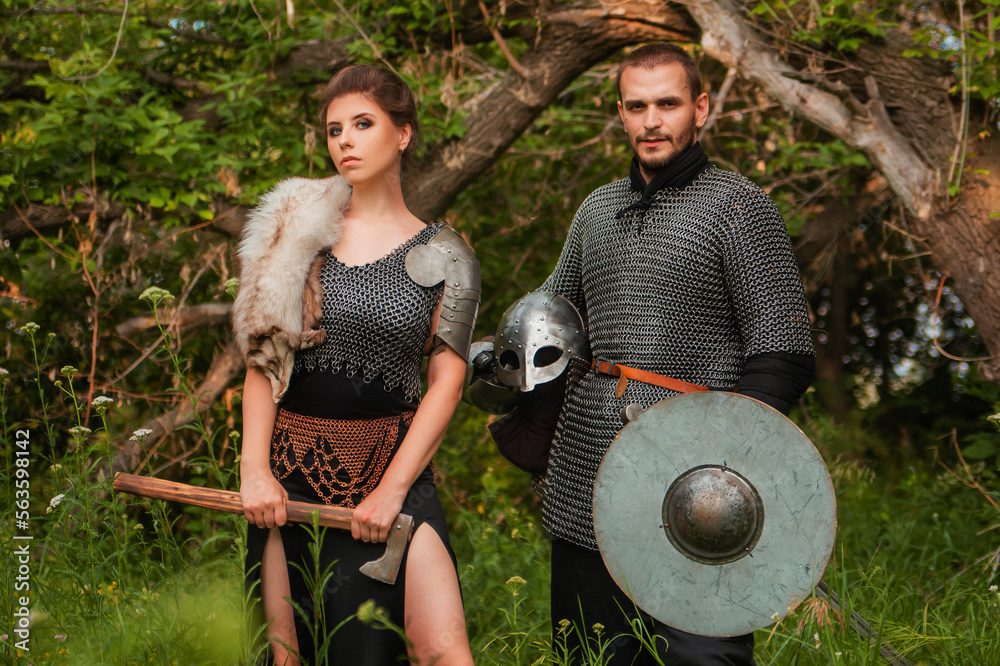 Young beautiful woman and man in armor, medieval warriors. A man in chain mail, a helmet with a ...