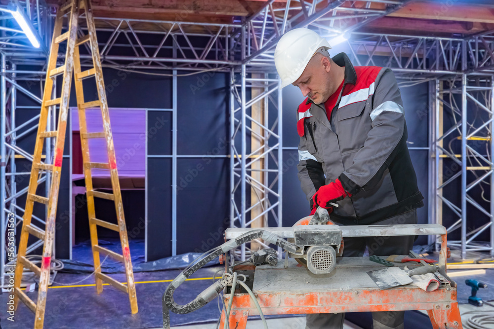 Man builder. Repairman in gray uniform. Man uses tile cutting machine ...
