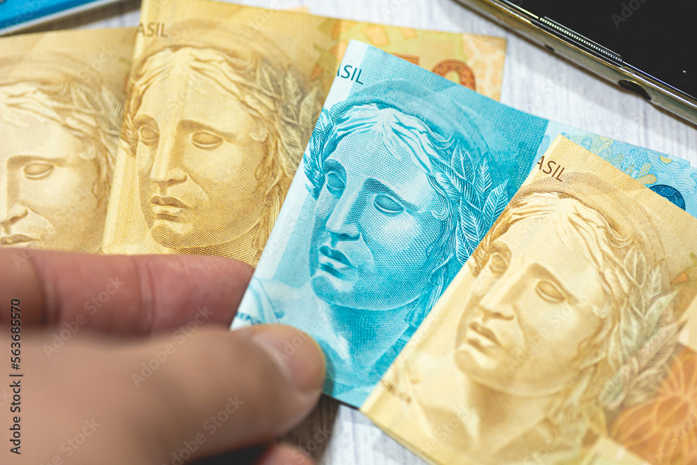 Um homem segurando uma nota do Real Brasileiro no valor de 100 Reais ...