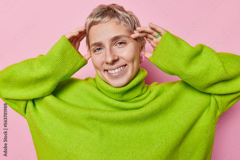 Beautiful cheerful woman with short haircut keeps hands on head smiles ...