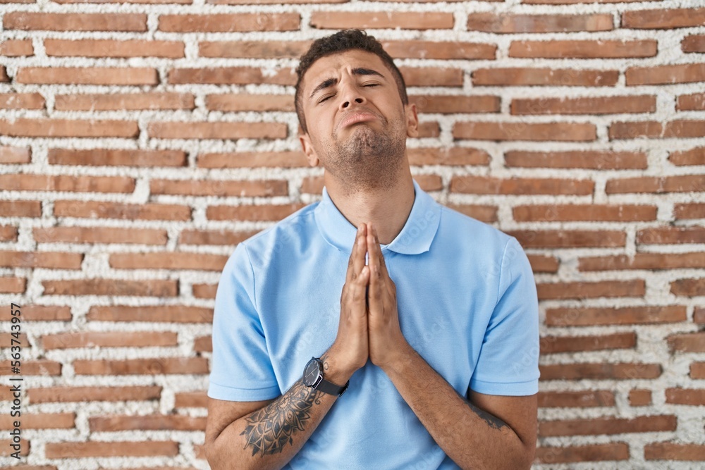Brazilian young man standing over brick wall begging and praying with ...