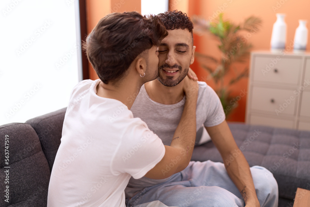 Two hispanic men couple sitting on sofa hugging each other and kissing ...