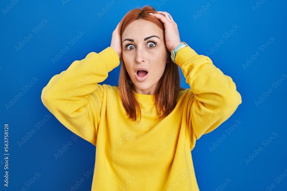 Young woman standing over blue background crazy and scared with hands ...