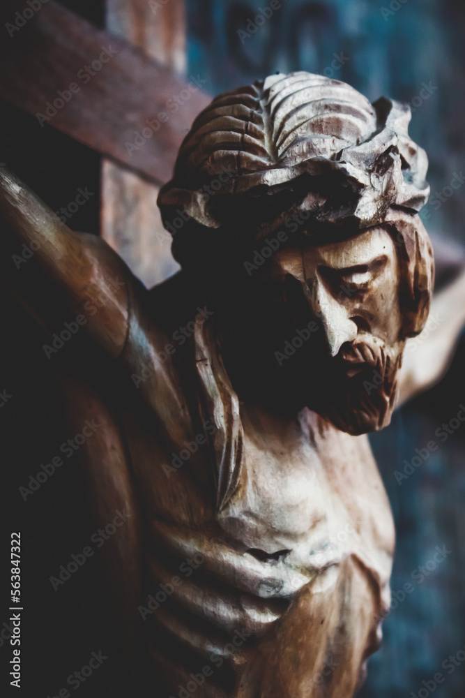 Jesus Christ crucified. Closeup fragment of an ancient wooden statue. Image with deep shadows ...