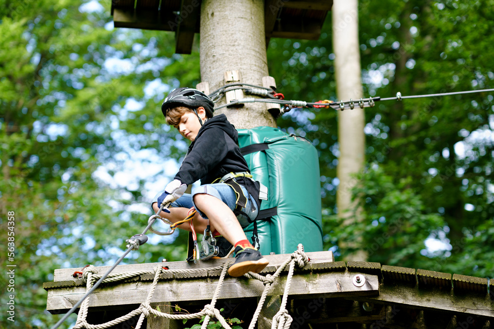 School boy in forest adventure park. Acitve child, kid in helmet climbs ...