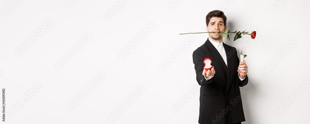 Romantic young man in suit making a proposal, holding rose in teeth and ...