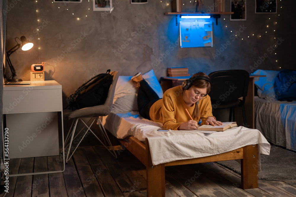 Female university or college student studying with textbooks on bed in ...
