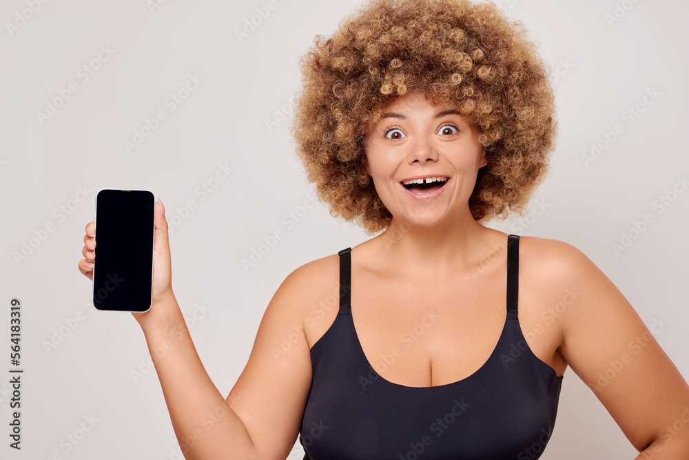 Horizontal shot of overjoyed curvy woman with curly hair in black top ...