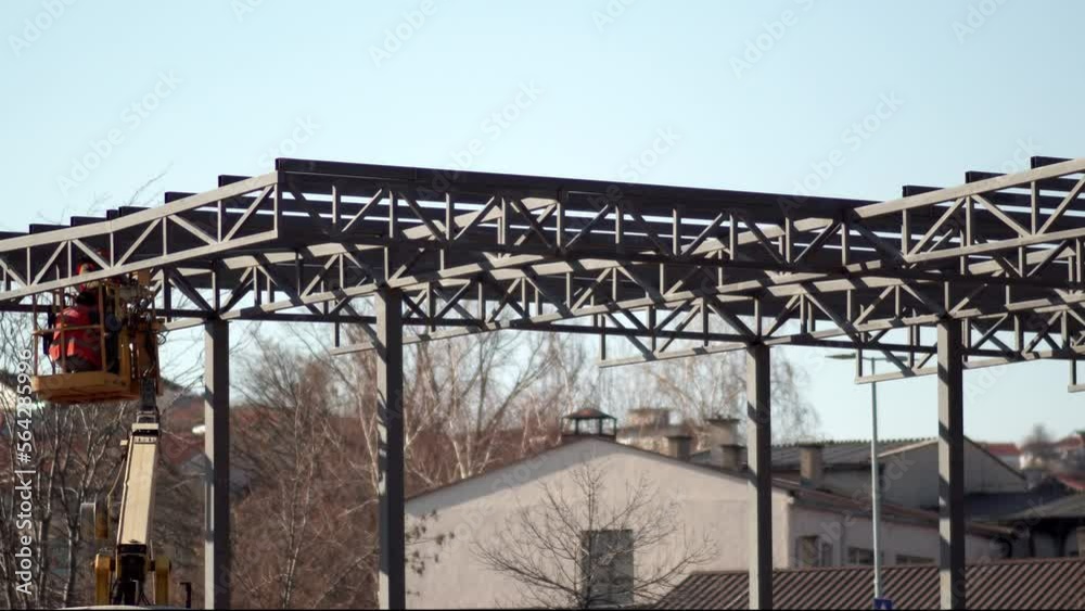 Workers on crane welding metal roof trusses installed by construction ...