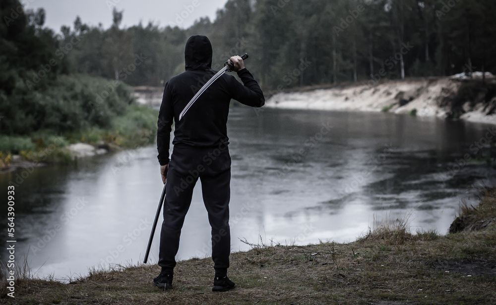 Foto de Back view. A man in black clothes holds a katana on his shoulder while standing with his ...