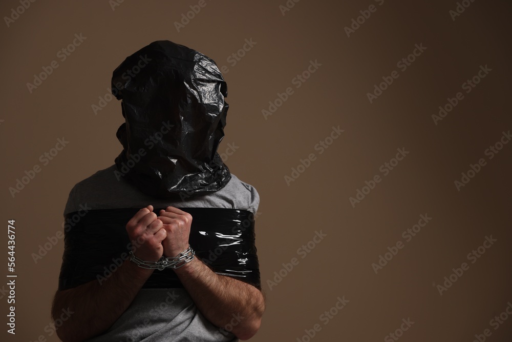 Tied man wrapped in black plastic bag on his head against dark ...