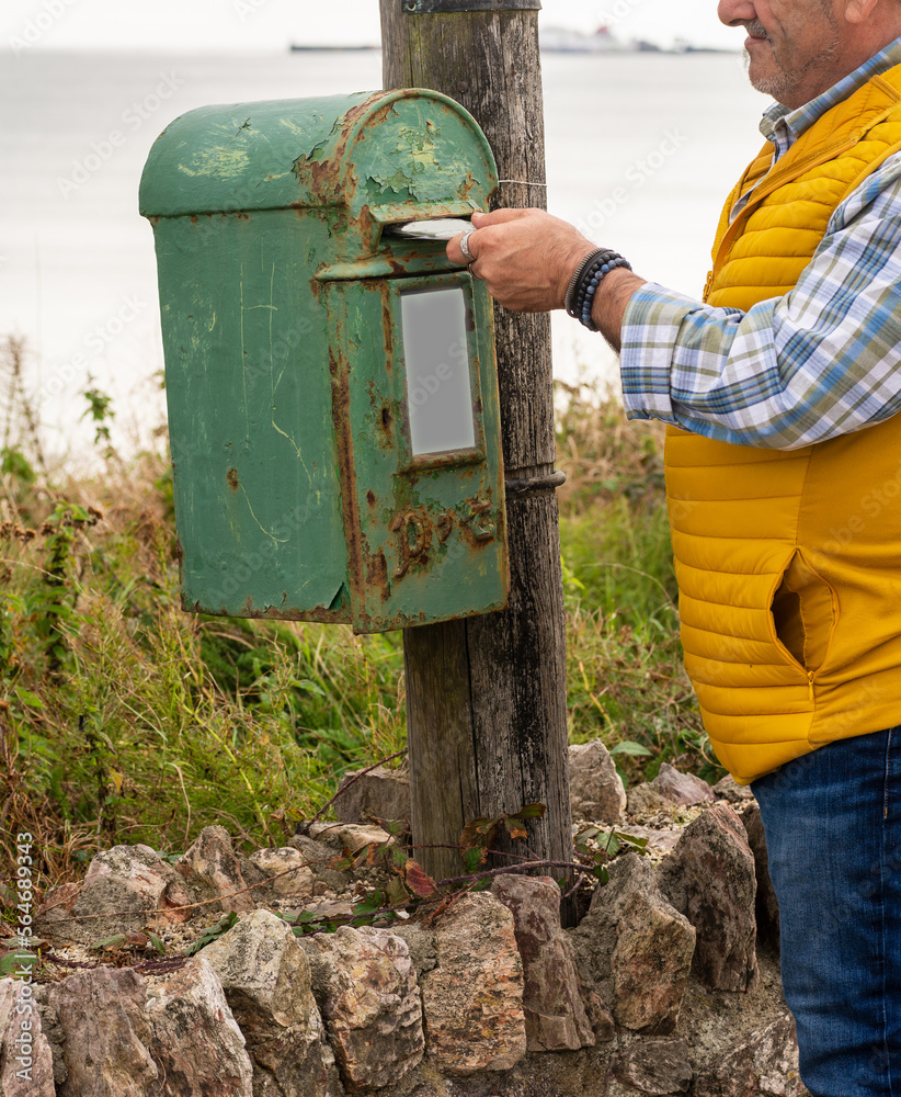 senior man putting letter in antique Irish mailbox, metal mailbox with ...