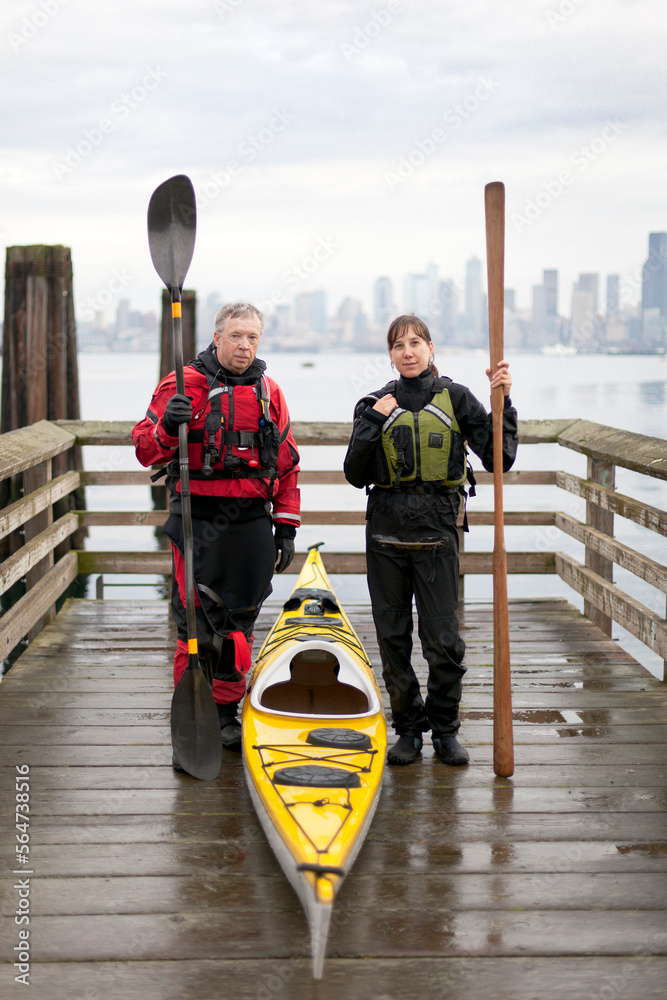 A modern senior male kayaker stands next to a traditional female ...