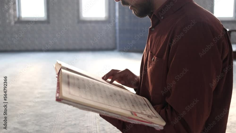Side view of a man reading the Islamic religious book Quran with his ...