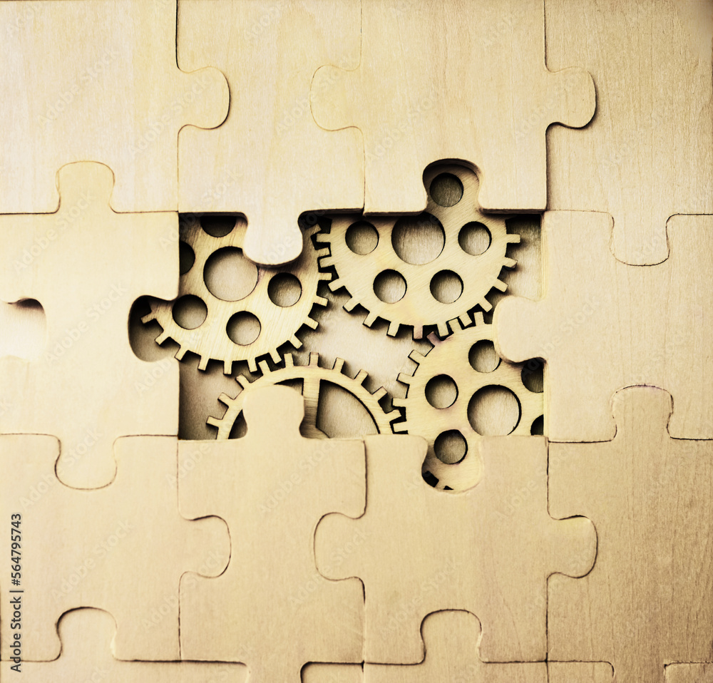 Cog wheels coming out from underneath a jigsaw puzzle. solving the ...